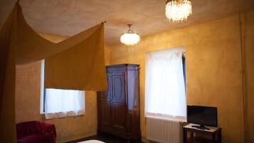 Quarto com uma cama, televisão sobre uma mesinha, armário e um candelabro.