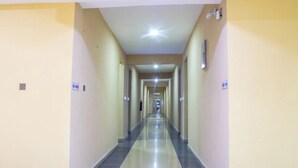 Um corredor comprido e estreito com piso refletivo, paredes em amarelo claro e teto com iluminação embutida.