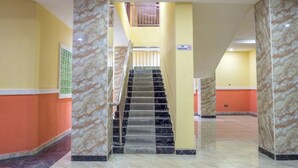 Um saguão de hotel com escadaria de mármore, um aviso de 'NÃO FUMAR' e vista para o andar superior.