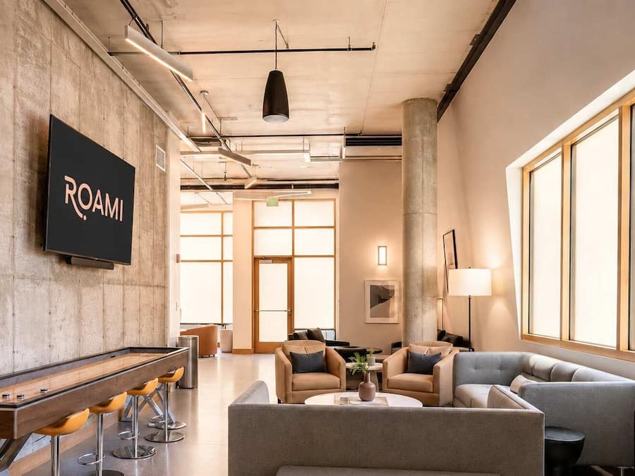 Uma área de estar moderna com um bar, assentos e uma tela de televisão exibindo 'ROAMI'.