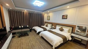 Quarto de hotel com duas camas, uma mesa, uma cadeira, uma televisão e um sofá.