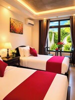 Quarto de hotel com duas camas, uma escrivaninha, uma cadeira, janela com cortinas e um quadro na parede.