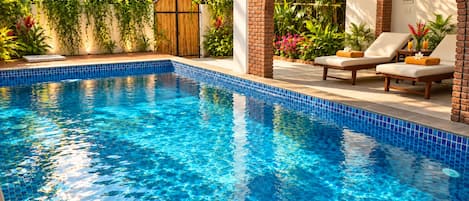 Piscina azul clara com bordas azulejadas, rodeada por um muro de tijolos e uma cerca de madeira.