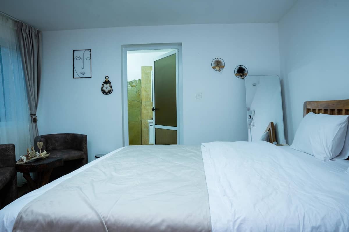 Quarto com cama, cadeira, mesinha, porta e espelho fixado na parede.