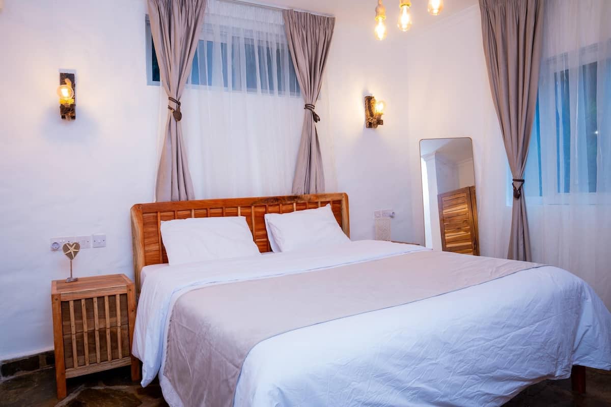 Cama bem arrumada com lençóis brancos, cabeceira de madeira e mesa de cabeceira com um objeto decorativo.