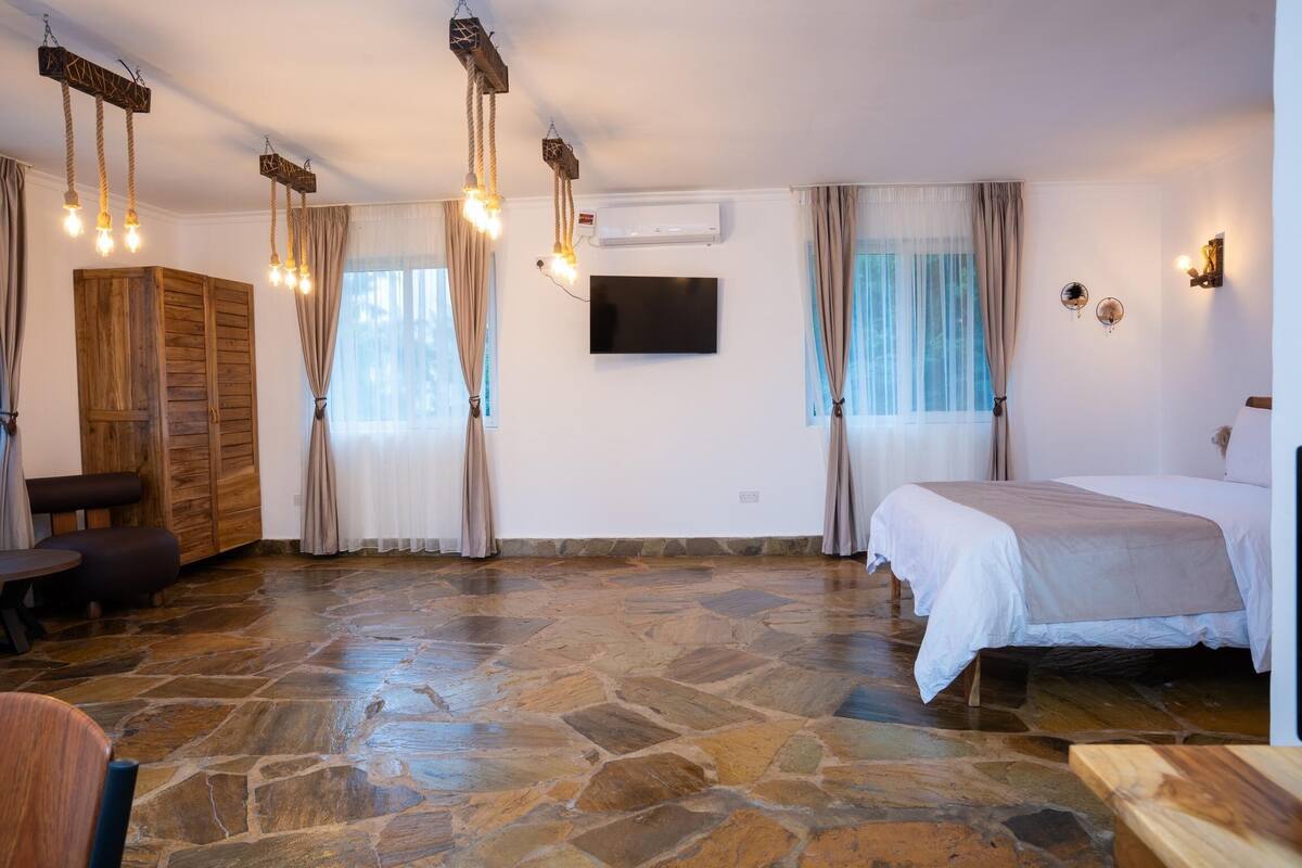 Quarto com chão de pedra, uma cama, televisão e guarda-roupa de madeira.