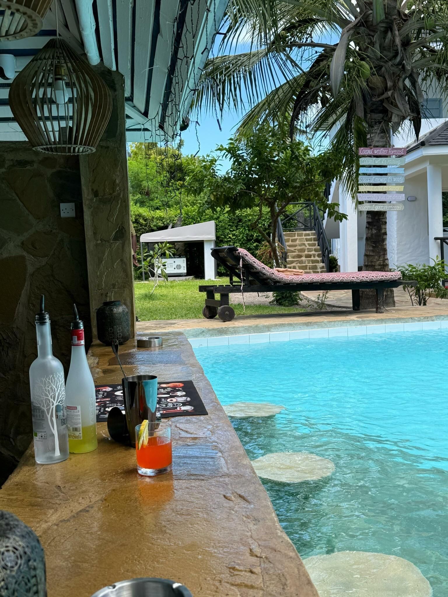 Um bar à beira da piscina com balcão de pedra, garrafas e uma bebida.