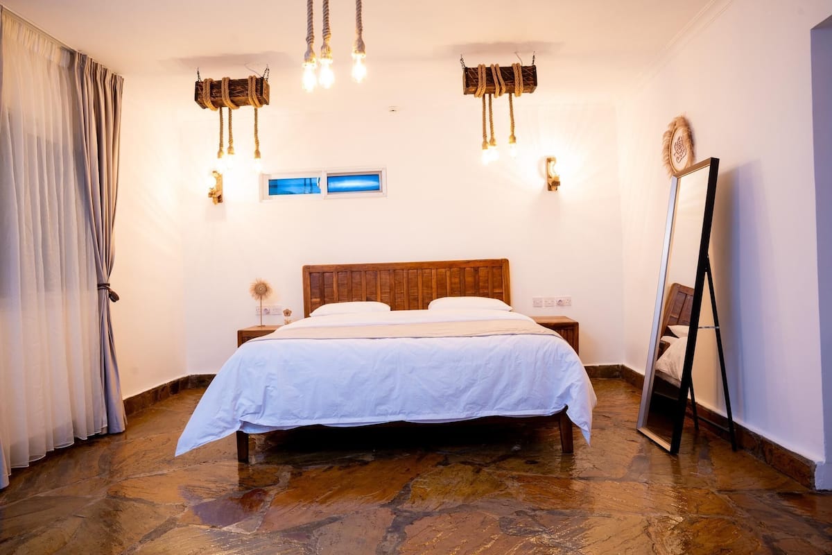 Um quarto com cama de madeira, piso de pedra, uma janela e um espelho.