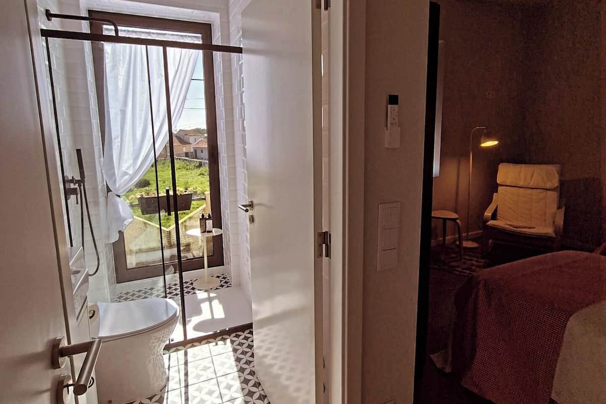 Quarto de hotel com banheiro, uma cama, mesa de cabeceira e abajur.