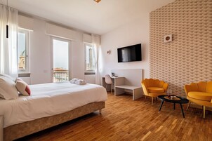 Quarto de hotel com cama, escrivaninha, duas cadeiras, televisão e vista para um edifício.