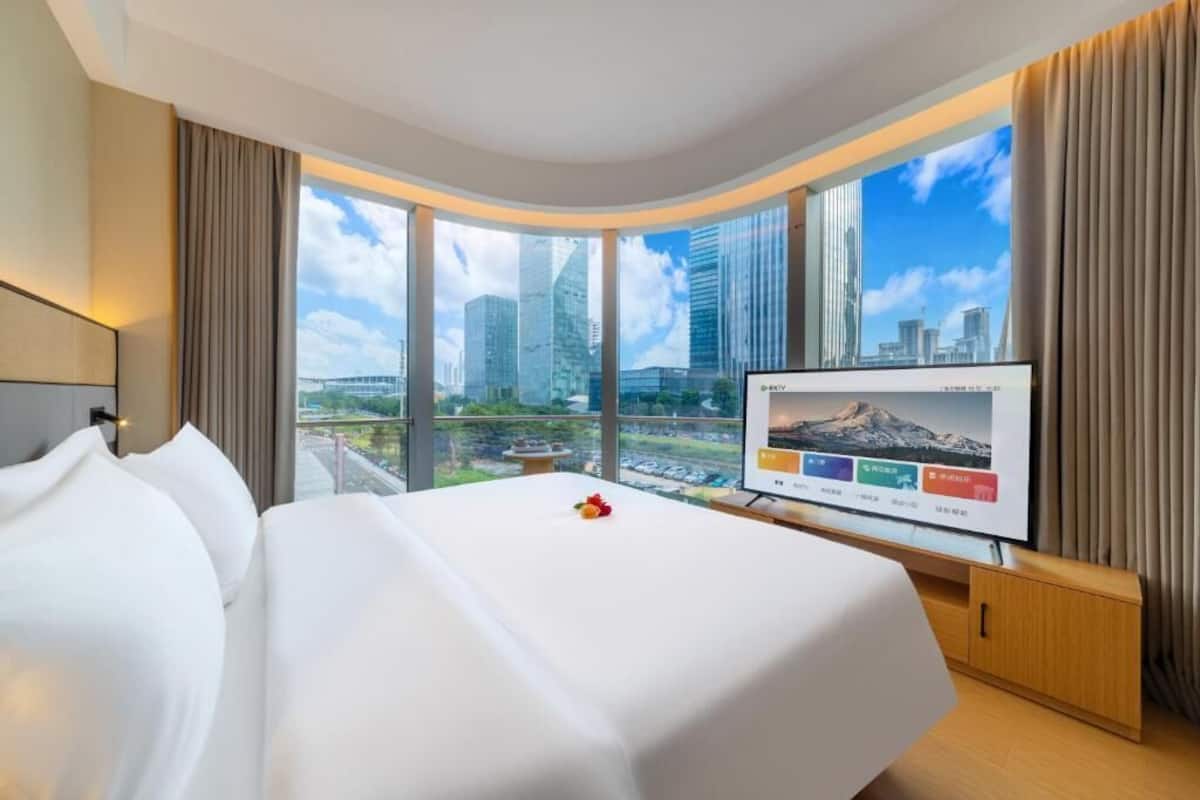 Quarto de hotel com uma cama grande, televisão de tela plana e vista para a cidade.