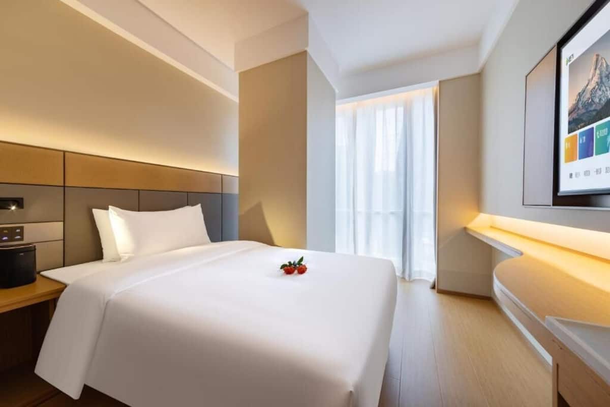 Quarto de hotel com cama, escrivaninha, televisão e janela com cortinas.