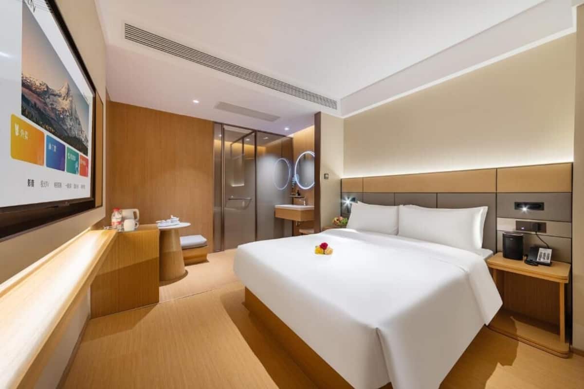 Quarto de hotel com uma cama grande, uma escrivaninha, uma toucador com espelho e um telefone fixado na parede.