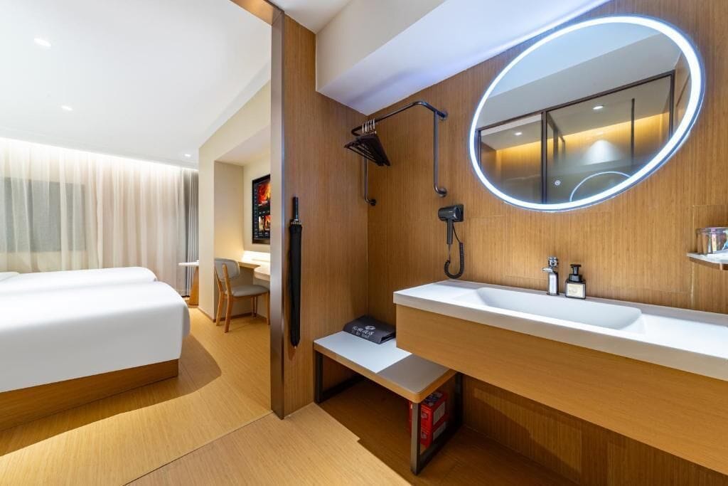 Quarto de hotel moderno com uma cama grande, banheiro com toucador, chuveiro e espelho.