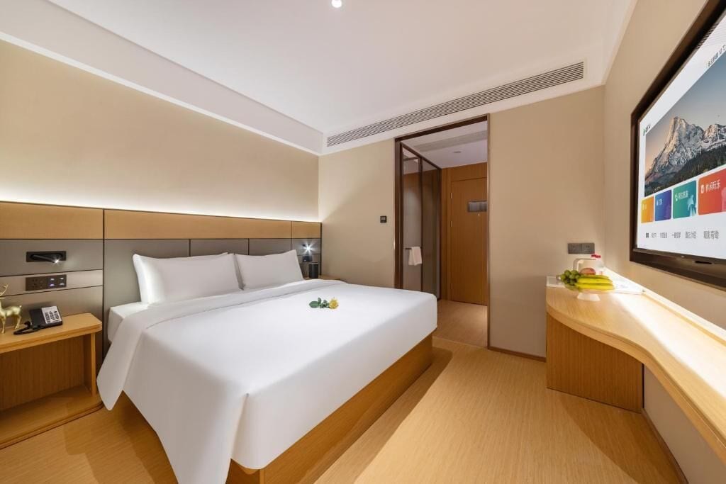 Quarto de hotel com cama, mesa de cabeceira e televisão na parede.