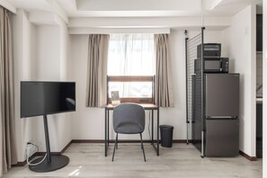 Quarto compacto com escrivaninha, cadeira, televisão de tela plana, micro-ondas e geladeira.
