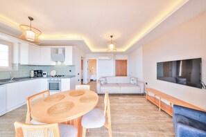 Cozinha moderna com armários brancos, uma mesa de jantar com cadeiras, um sofá, uma TV e um banco.