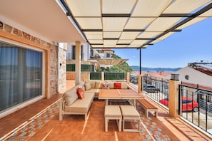 Uma varanda com sofá, mesa e cadeiras, com vista para uma rua com carros e edifícios.