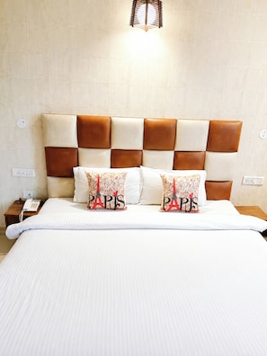 Quarto de hotel com cabeceira quadriculada, cama com roupa de cama branca e duas almofadas decorativas com o texto 'PARIS'.