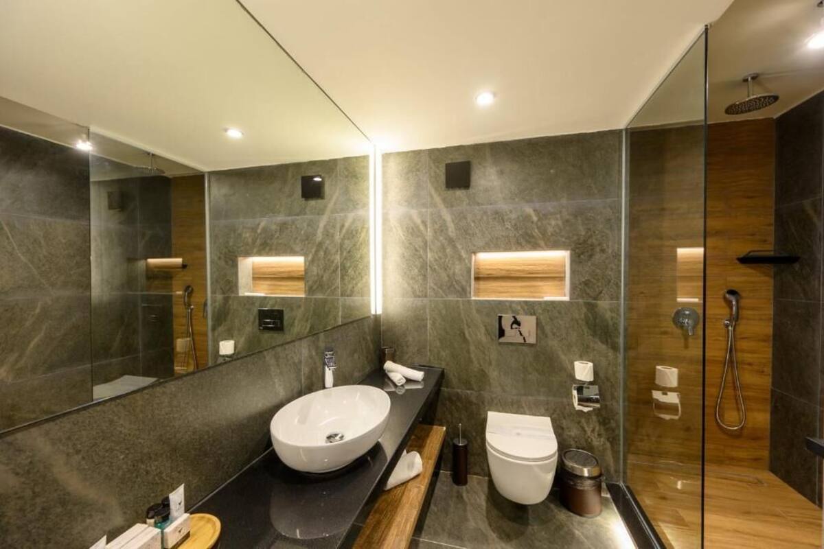 Uma casa de banho moderna com um espelho grande, lavatório suspenso, sanita e cabine de duche com parede de vidro.