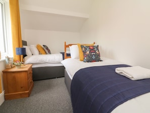Quarto com duas camas, mesa de cabeceira, abajur e janela com cortinas.