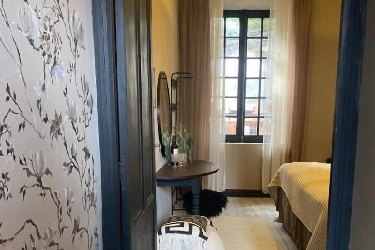 Um corredor estreito com uma cama, um espelho e uma janela com cortinas.