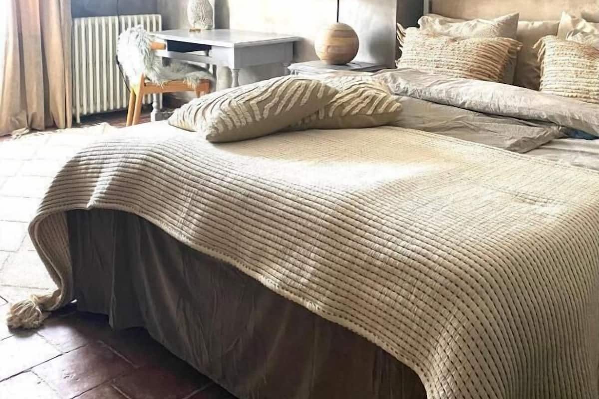 Quarto com uma cama grande, uma escrivaninha com abajur, uma cadeira e um radiador.