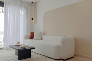 Uma sala de estar moderna com um sofá branco, uma mesa de centro preta e uma luminária de anel na parede.