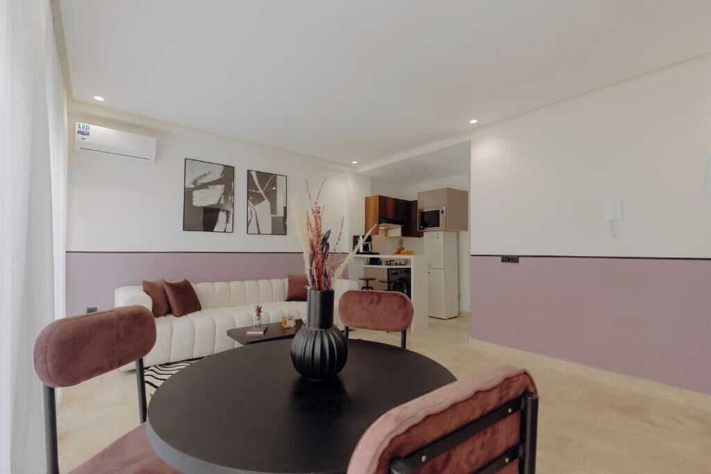 Uma sala de estar moderna com uma mesa redonda, um sofá e uma cozinha ao fundo.