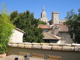 Terraço com mesa e cadeiras, com vista para um edifício histórico com torre e estrutura semelhante a um castelo.