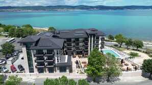 Um hotel com vários andares, piscina, estacionamento e vista para o mar.