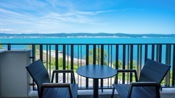 Varanda com duas cadeiras e uma mesa pequena, com vista para o horizonte costeiro.