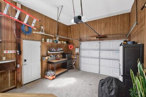 Uma garagem com uma bancada de trabalho, prateleiras com ferramentas, uma escada e uma porta de garagem.
