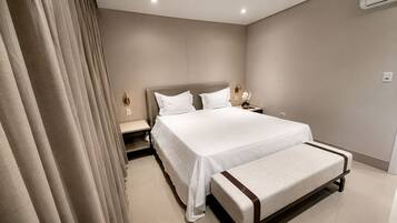 Quarto de hotel moderno com cama grande, mesas de cabeceira e um banco.