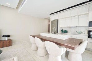 Uma cozinha moderna com uma ilha central, armários brancos e uma longa mesa de jantar com cadeiras combinando.