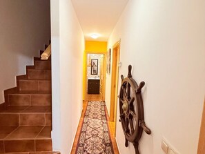 Um corredor com carpete estampado, escada de madeira e decoração de roda de navio na parede.