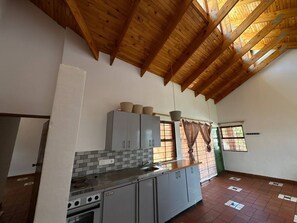 Uma cozinha com painel de azulejos, vigas de madeira no teto, fogão e armários.