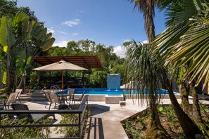 Uma área de piscina com espreguiçadeiras, um espaço de estar coberto e um elemento decorativo com água.
