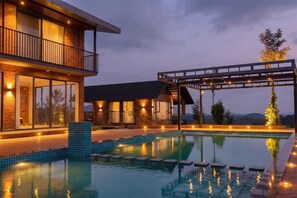 Um edifício moderno de dois andares com piscina, iluminação externa e uma área coberta com vista para a paisagem.