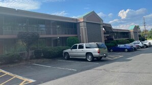 Um estacionamento com vários carros, um edifício com grandes janelas e céu aberto.