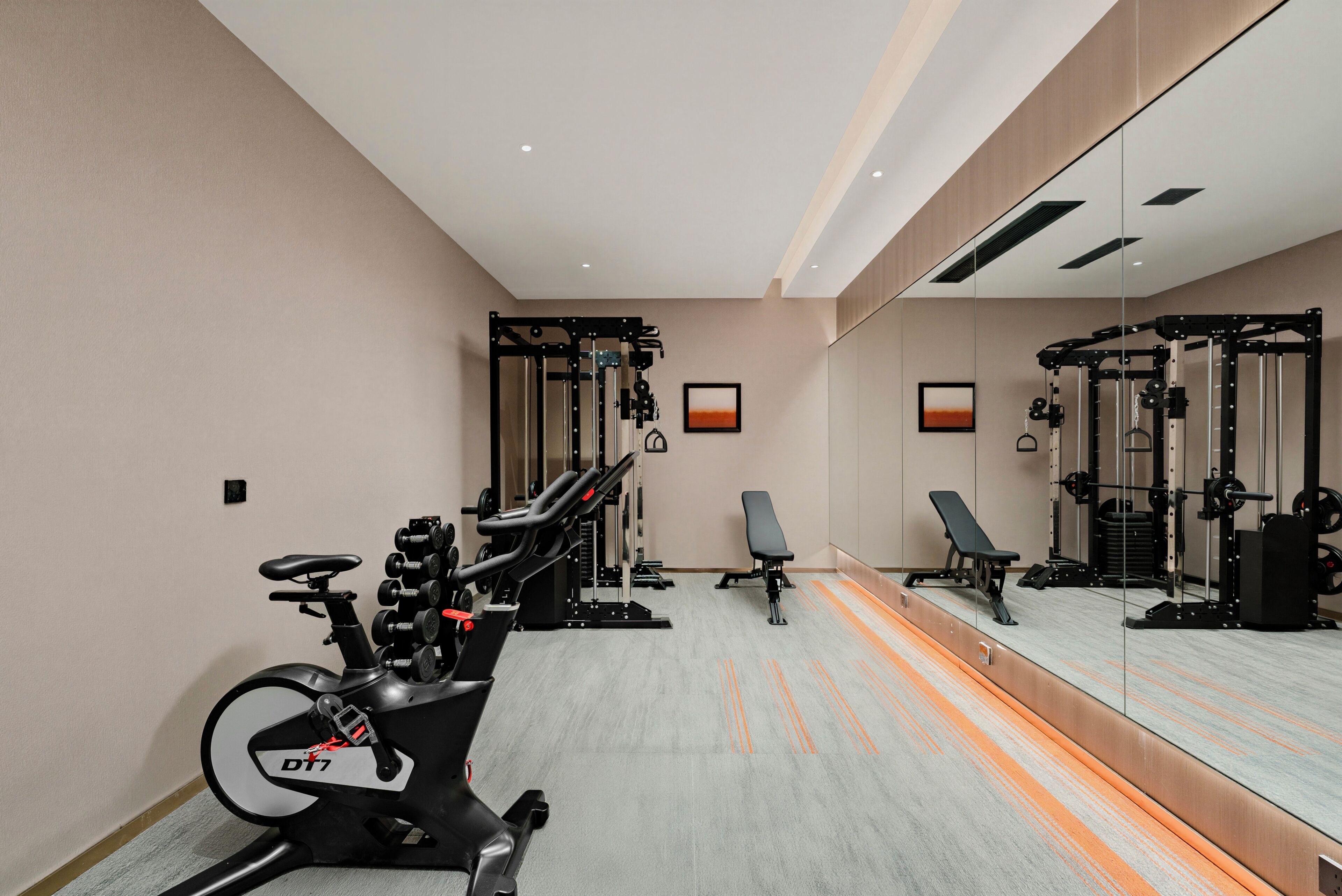 Academia com equipamentos de ginástica, um banco e um espelho grande na parede.