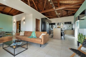 Uma sala de estar moderna com um sofá, mesa de centro e uma cozinha ao fundo.