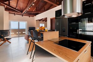 Cozinha moderna com ilha central, eletrodomésticos de aço inoxidável e teto de madeira.
