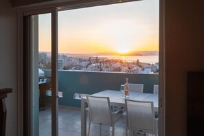 Varanda com mesa e cadeiras, vista para um horizonte urbano ao pôr do sol.