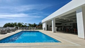 Piscina com espreguiçadeiras, área de estar coberta e vista para a paisagem ao redor.