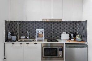 Uma cozinha compacta com micro-ondas, cafeteira, torradeira e uma pia pequena.
