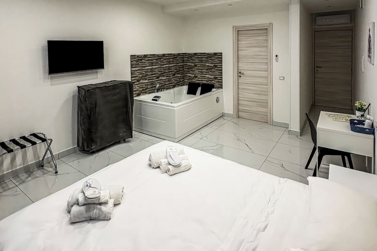 Quarto de hotel moderno com uma cama grande, televisão de tela plana, uma escrivaninha pequena e área de chuveiro.