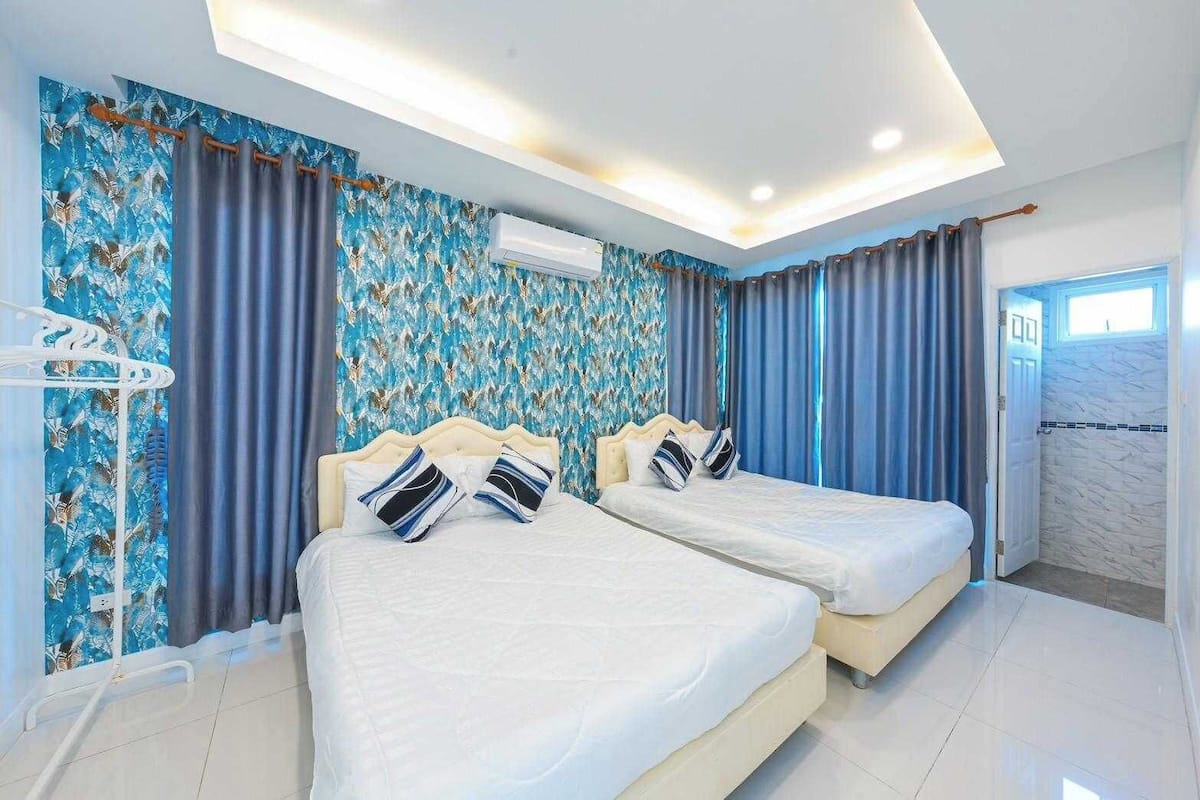Quarto de hotel com duas camas, uma luminária no teto, ar condicionado e banheiro com chuveiro.