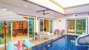 Piscina interna com escorregador, cadeiras de descanso e mesa de bilhar.
