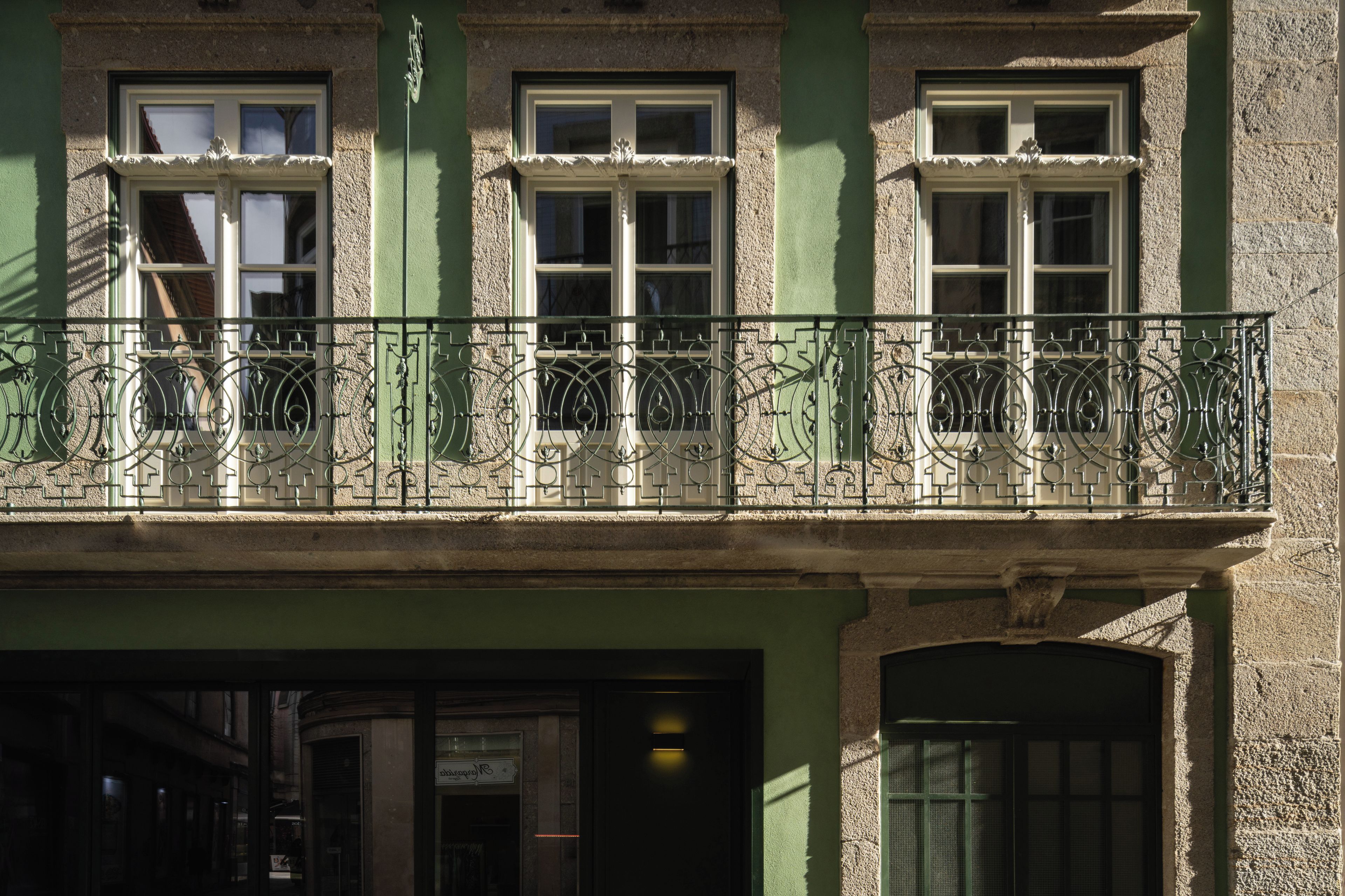 Um edifício com fachada verde, várias janelas e uma varanda com grades de metal decorativas.